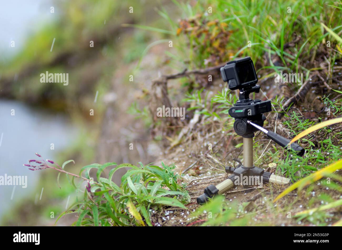 Action camera on a small tripod stands in the grass of the river under ...
