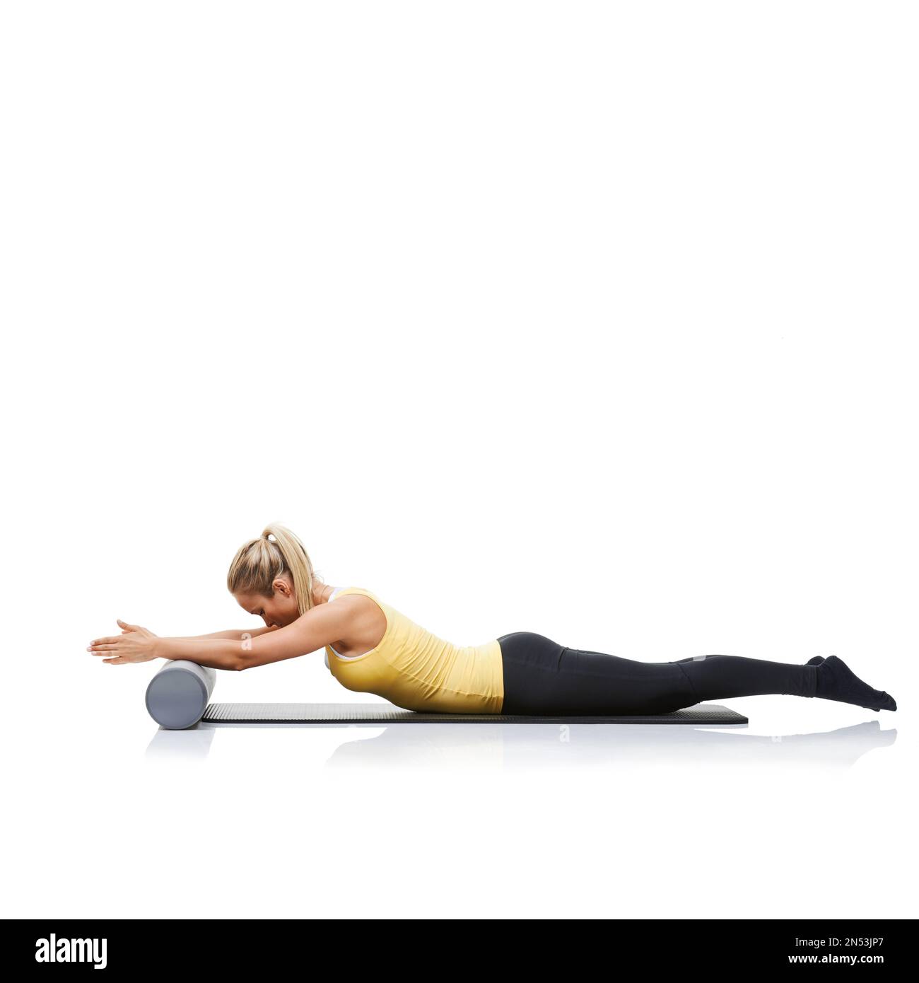 Face down on her exercise mat. A young woman using a foam roller to ...