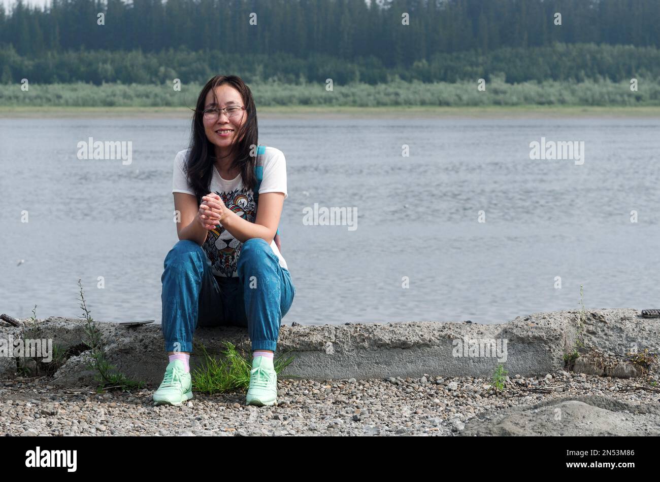 Smiling sports Yakut Asian young girl sitting on the stone Bank of the ...