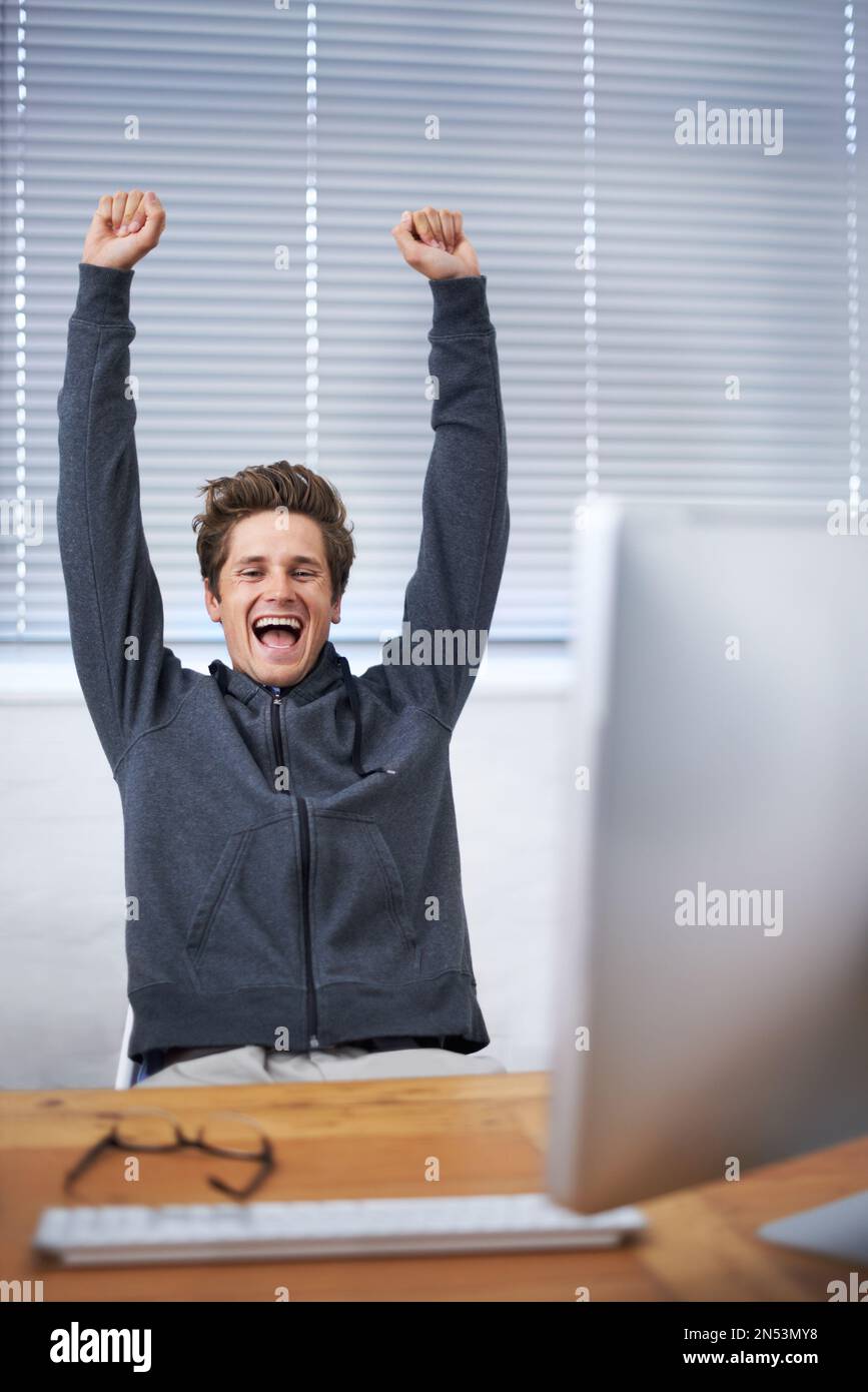 Success feels so good. A handsome young man celebrating at his desk ...