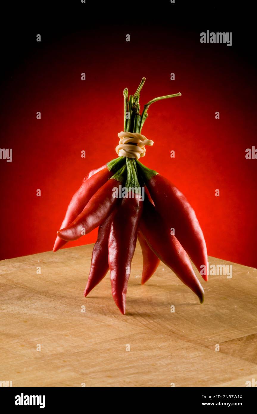 Bunch of red chilli peppers sitting on a timber bench Stock Photo - Alamy