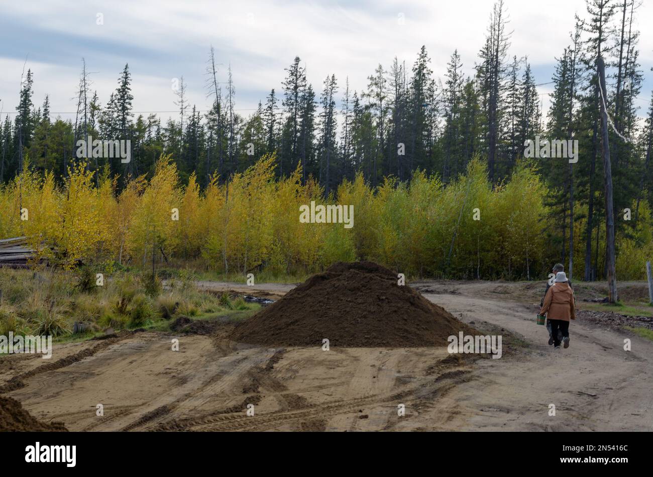 A pair of elderly Yakuts walk past a large pile of clay and earth to ...