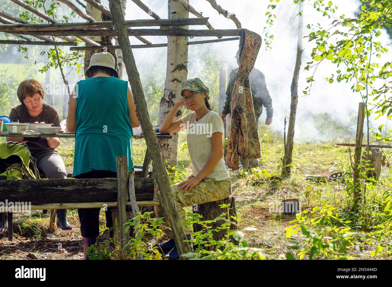 Yakut family bright day in the woods at a wooden table preparing dinner ...
