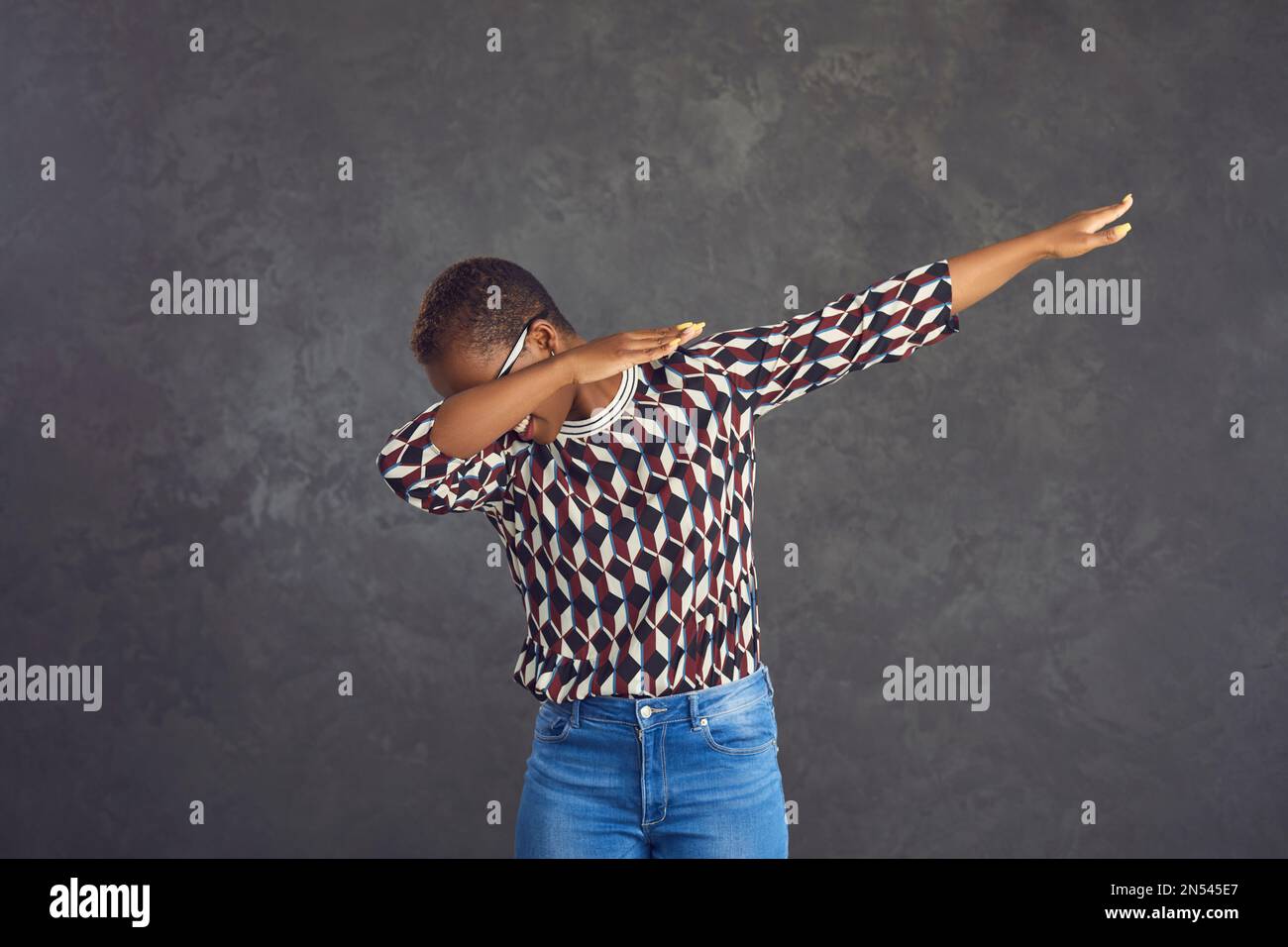 Funny happy young African woman dancing dab isolated on grey concrete ...