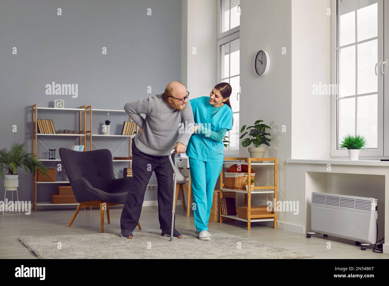 Smiling caregiver or nurse helping a retired senior man who's walking ...