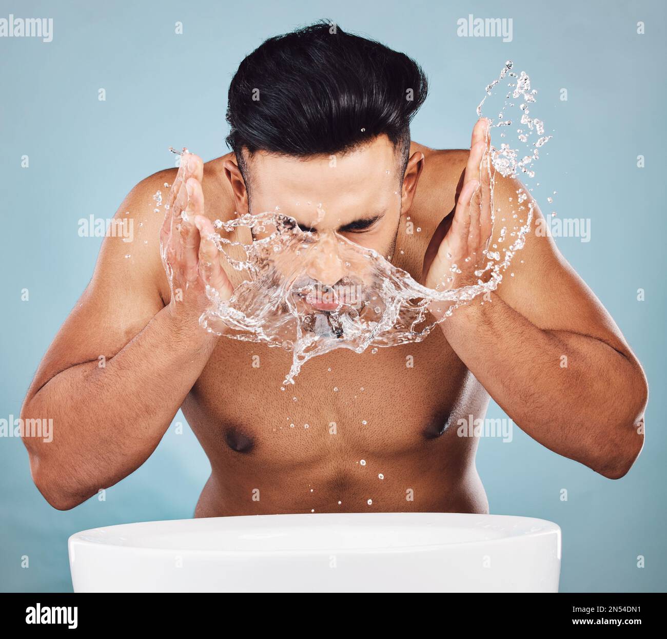 Man, water splash and face wash by basin for skincare, fresh clean hygiene or grooming against a ...