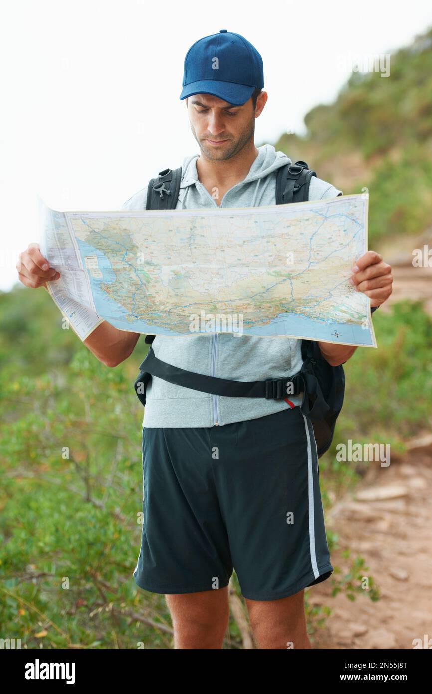 Plotting his next move. Handsome young hiker reading a map while ...