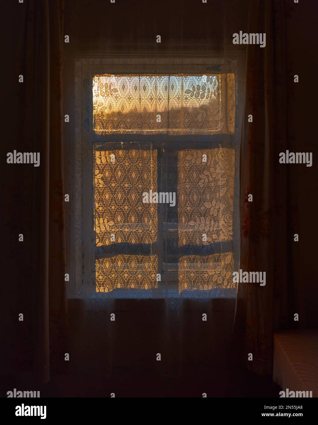 A dark, rustic room with a corner table and a window behind a curtain ...