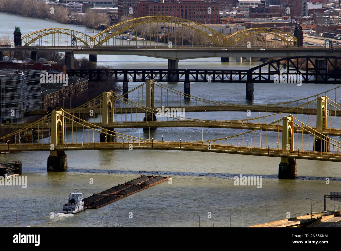 A towboat and barges make their way up the Allegheny River under three historic bridges named ...