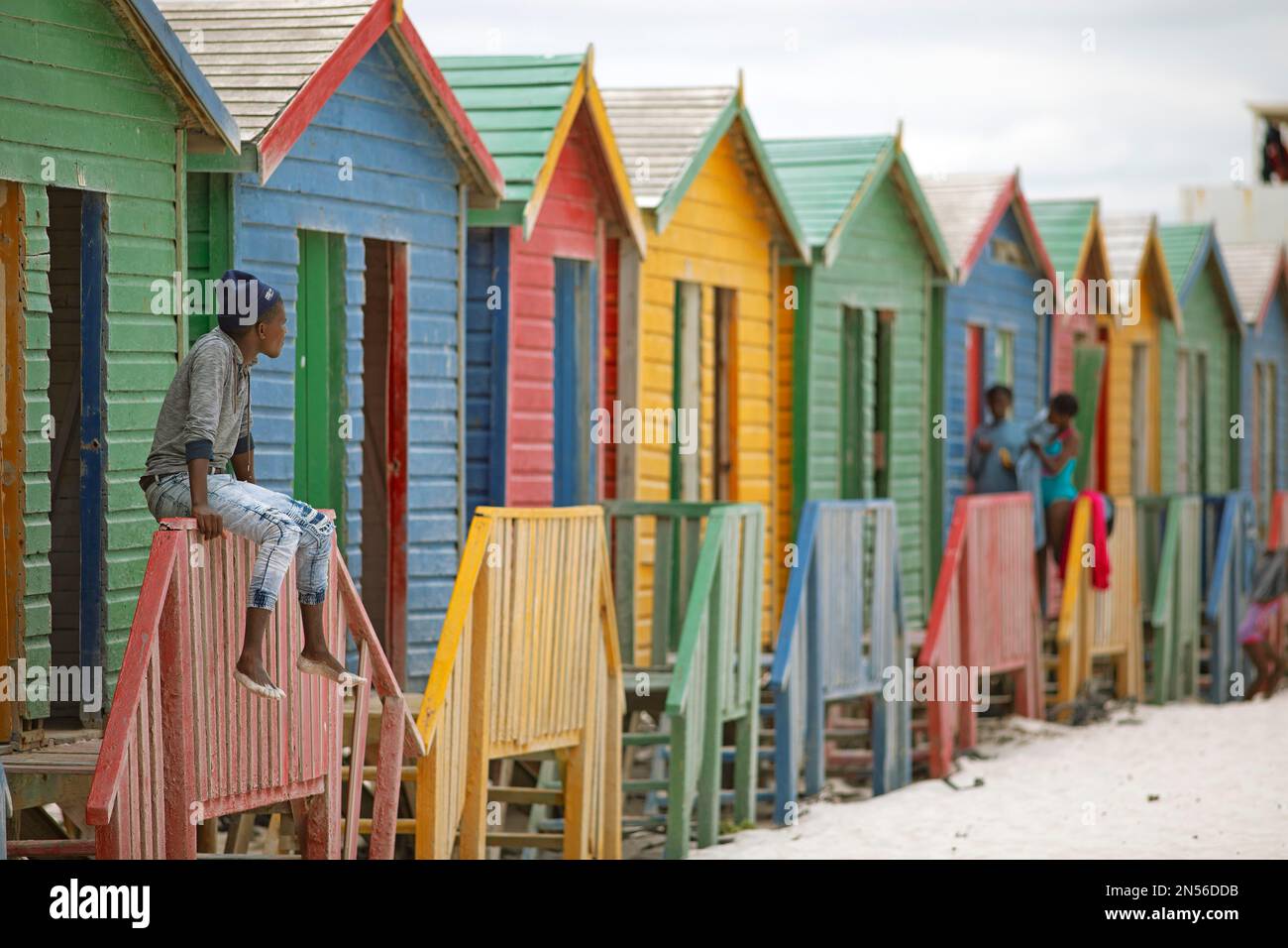 Man sitting on fence in front of colourful beach huts, Muizenberg ...