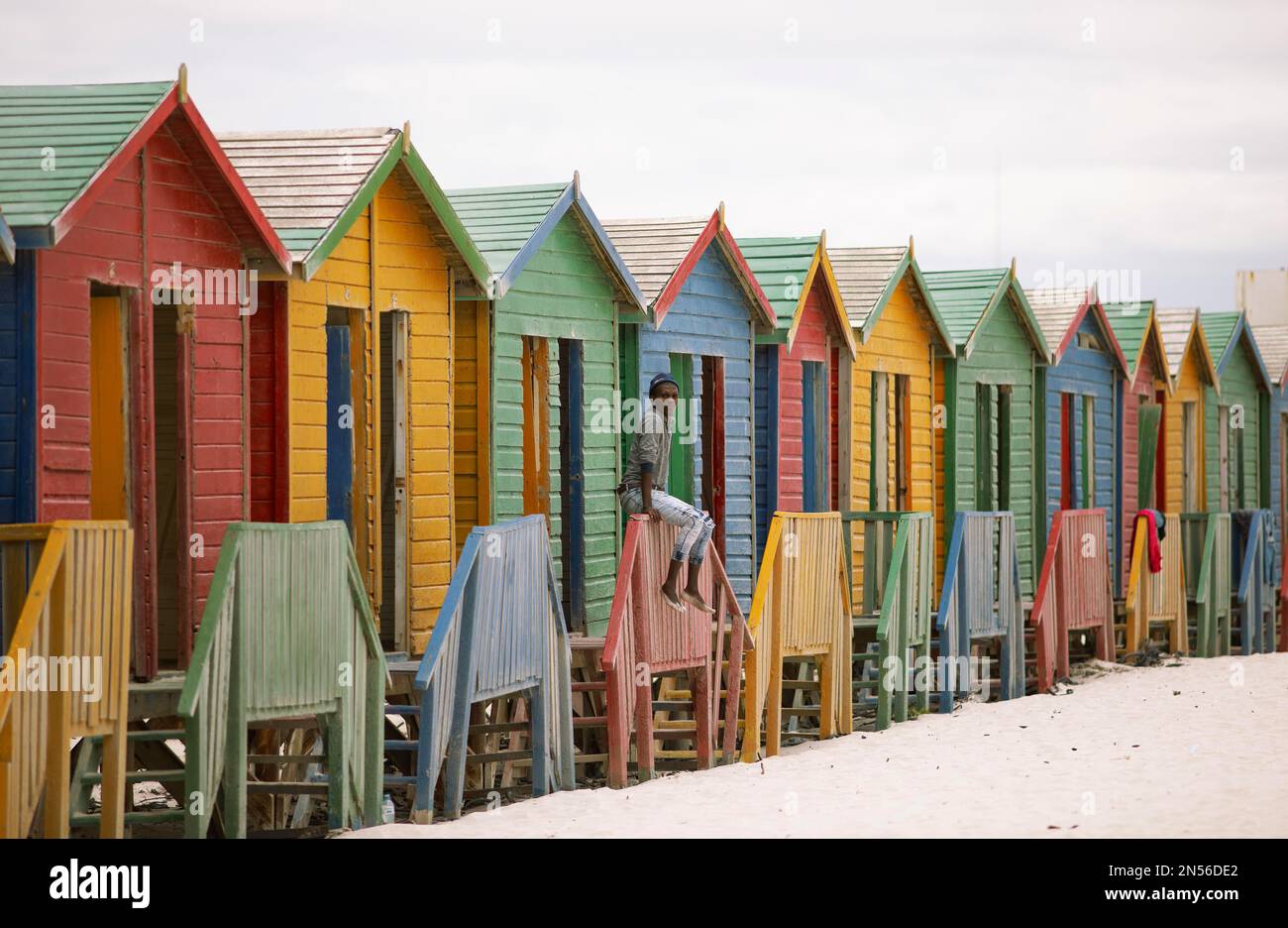 Man sitting on fence in front of colourful beach huts, Muizenberg ...