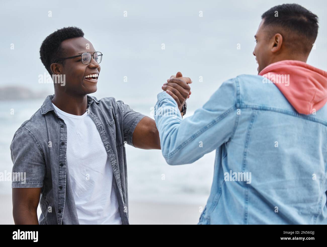 Friends, handshake and greet at a beach while on vacation, holiday or ...