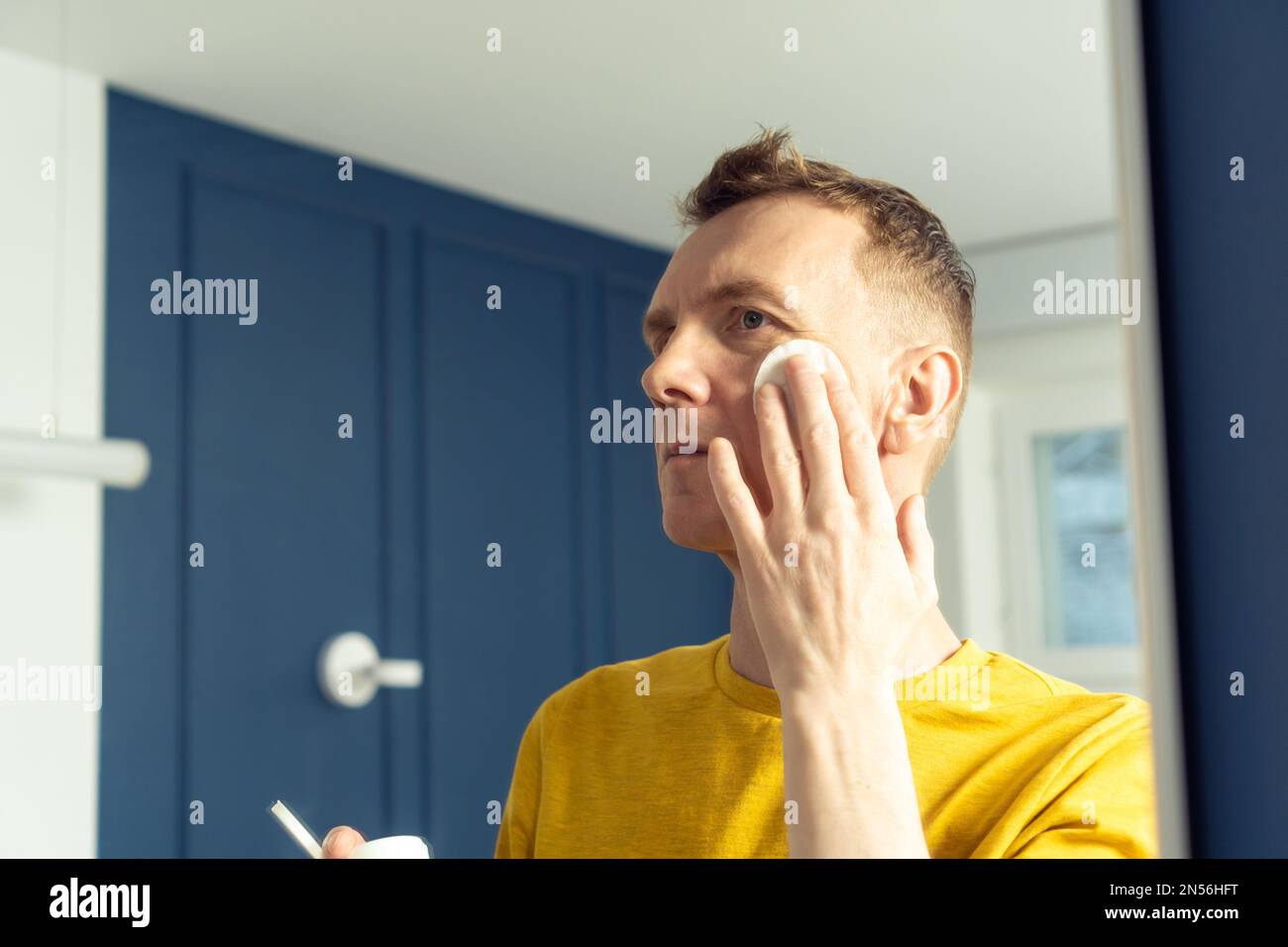 Adult man apply face tonic with cotton pad, then massage with hands ...