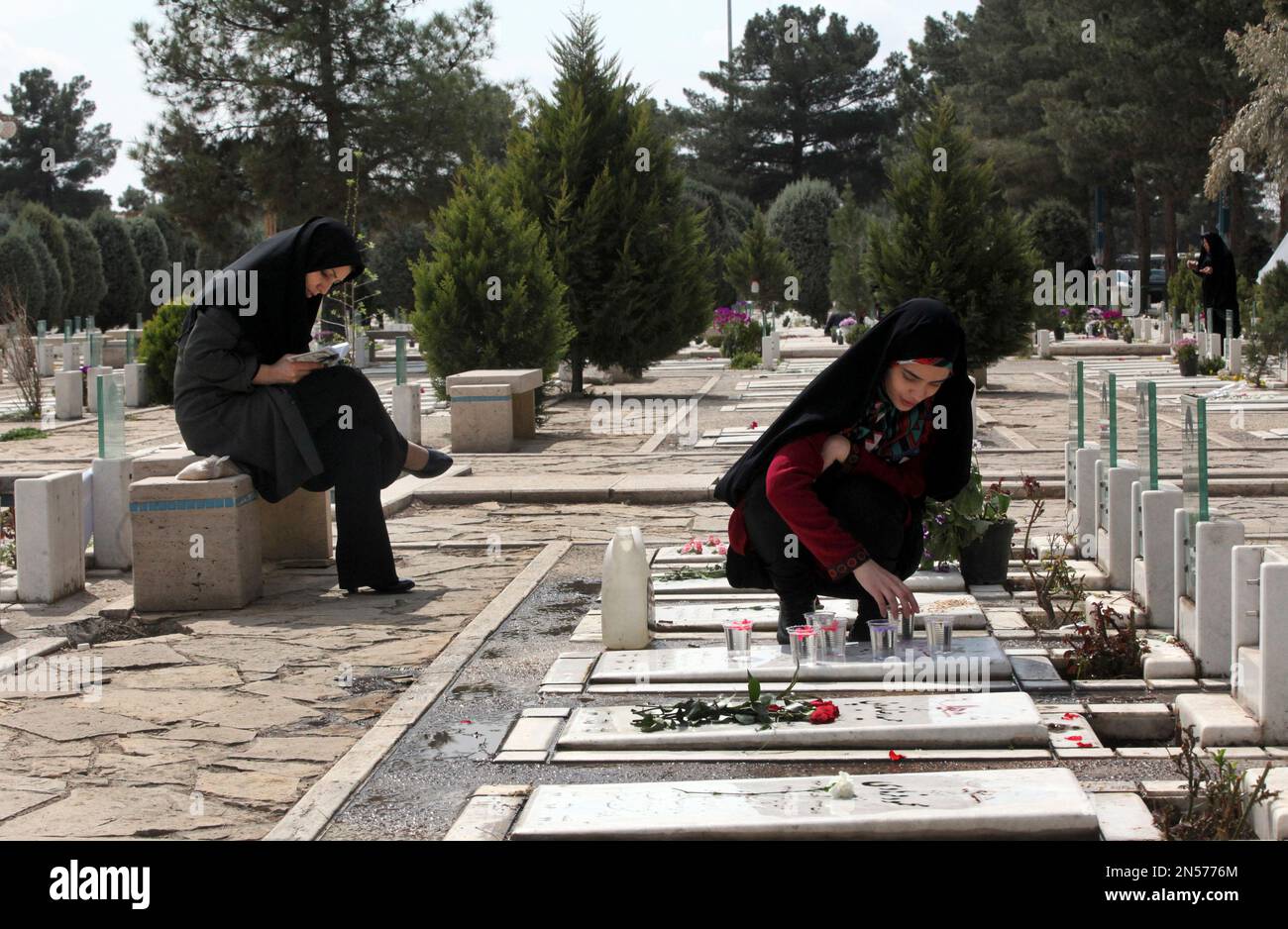 An Iranian woman prays as another decorates the graves of soldiers who ...