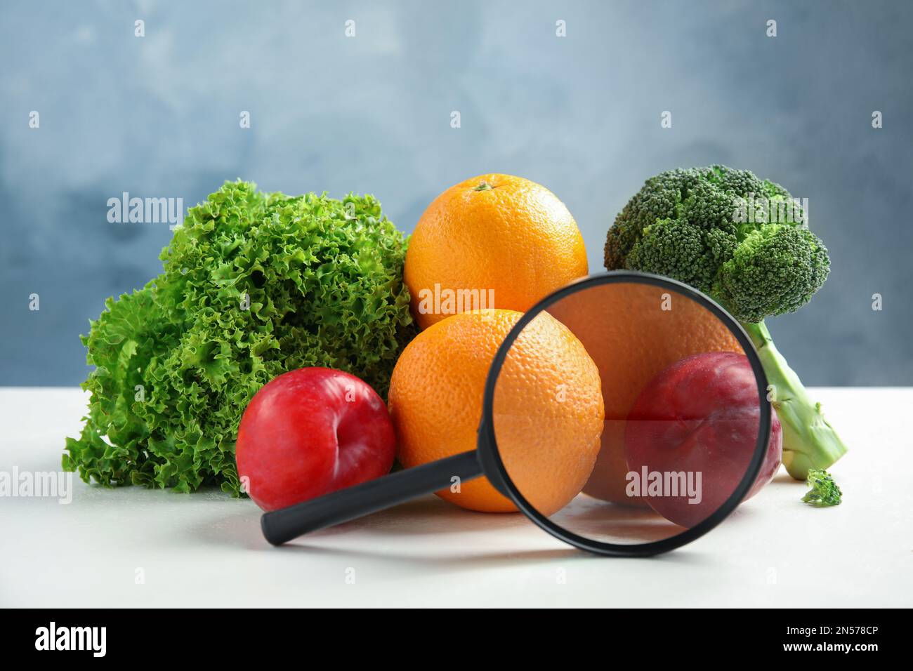 Fresh fruits, vegetables and magnifying glass on white table against ...