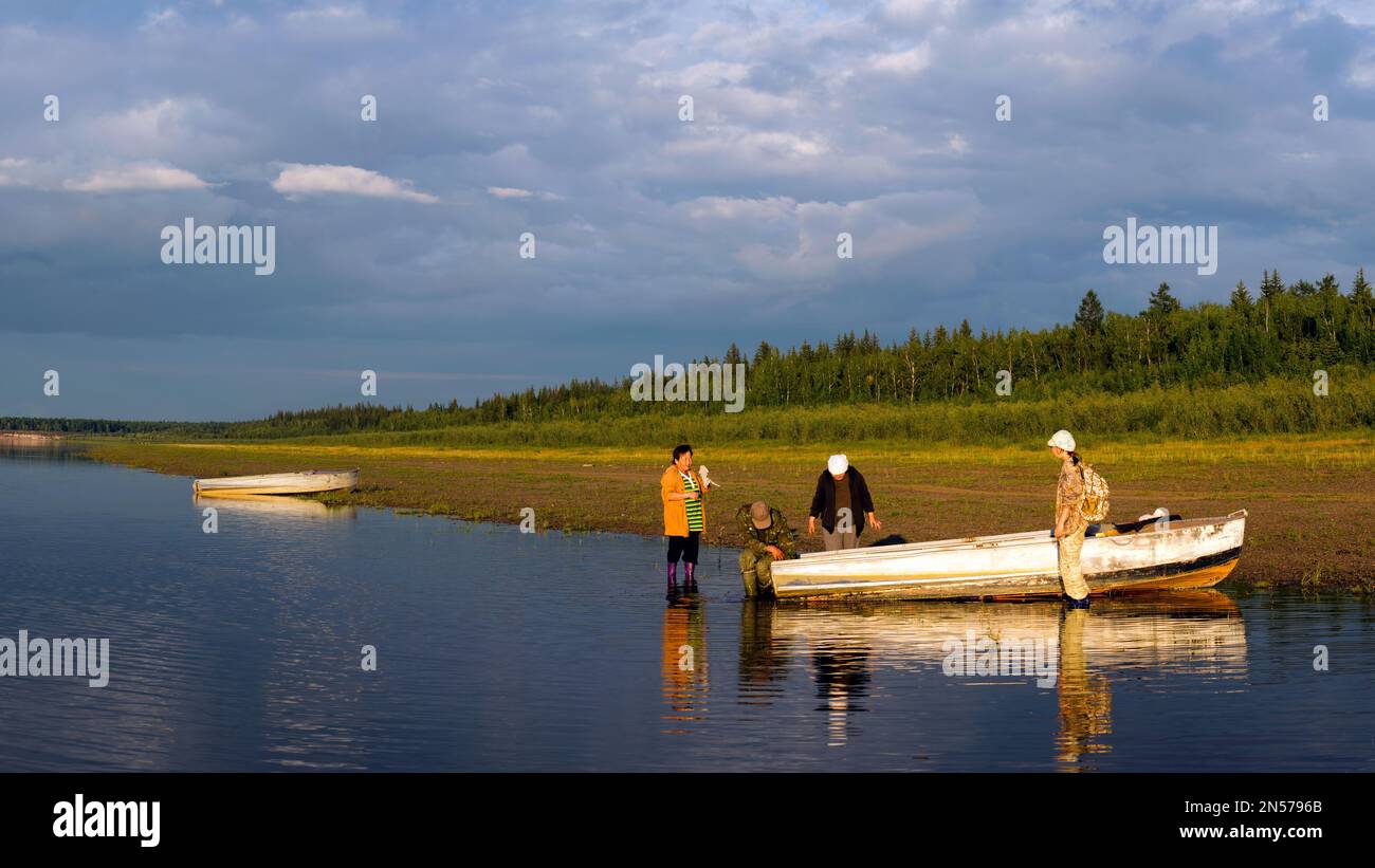 Three Yakut women and one Yakut man tinkering at a boat on the banks of ...
