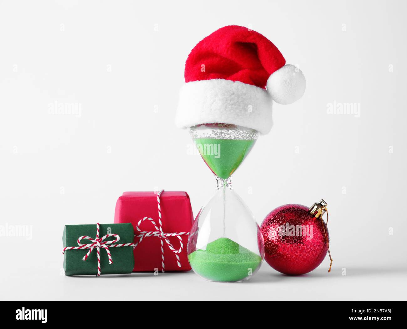 Hourglass with Santa hat and festive decor on white background ...