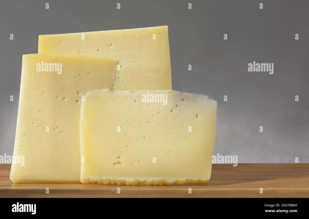 Three pieces of hard cheese on a gray background in a horizontal format ...
