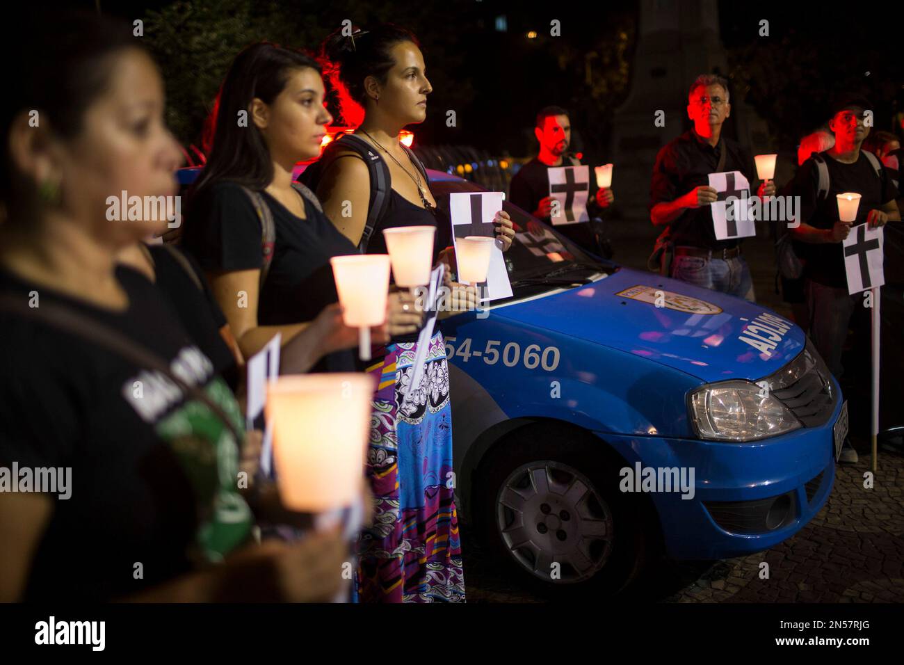 People hold candles and images of a cross near a police car during a ...