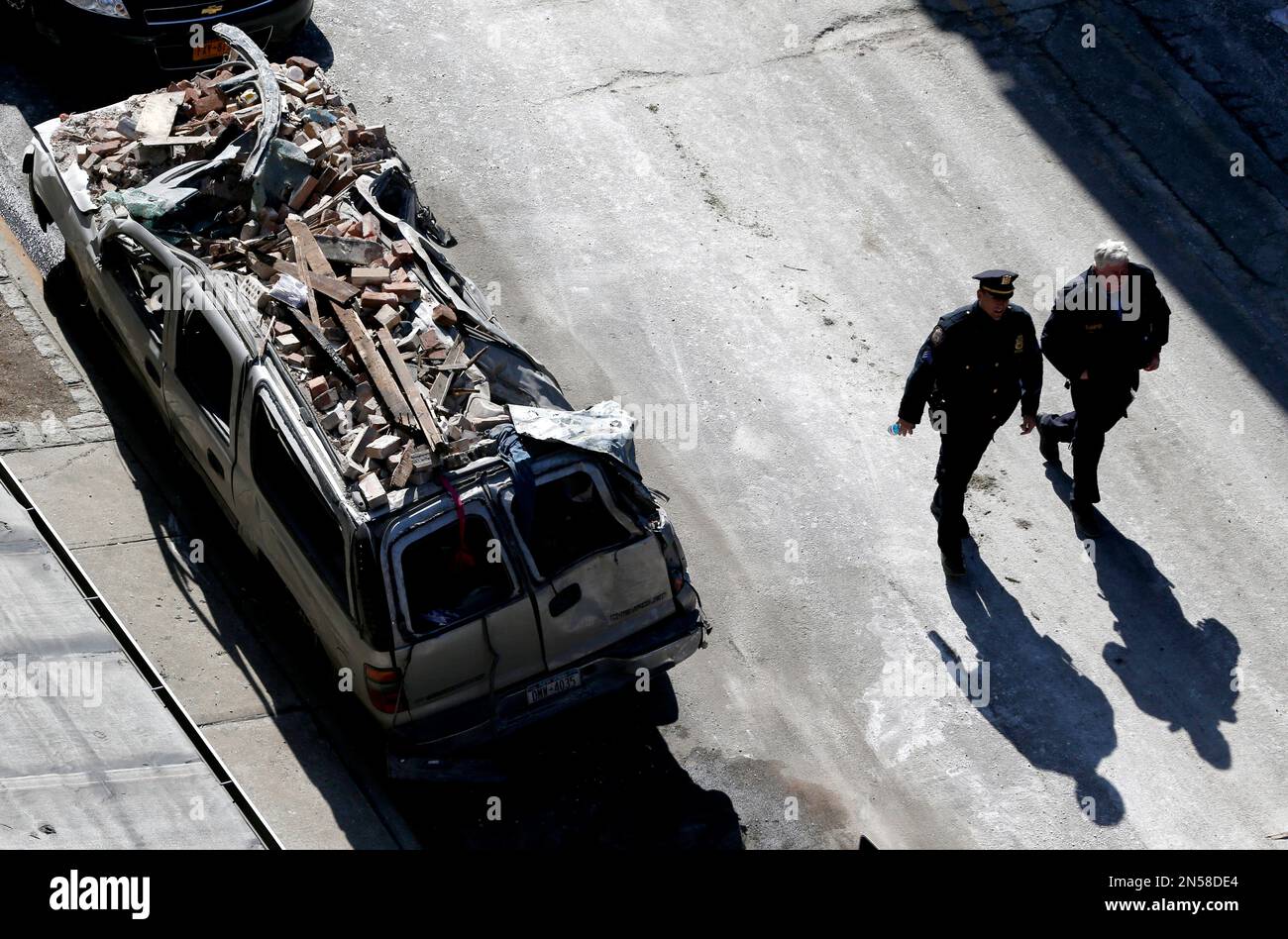 Two police officers walk near a vehicle that was crushed under debris ...
