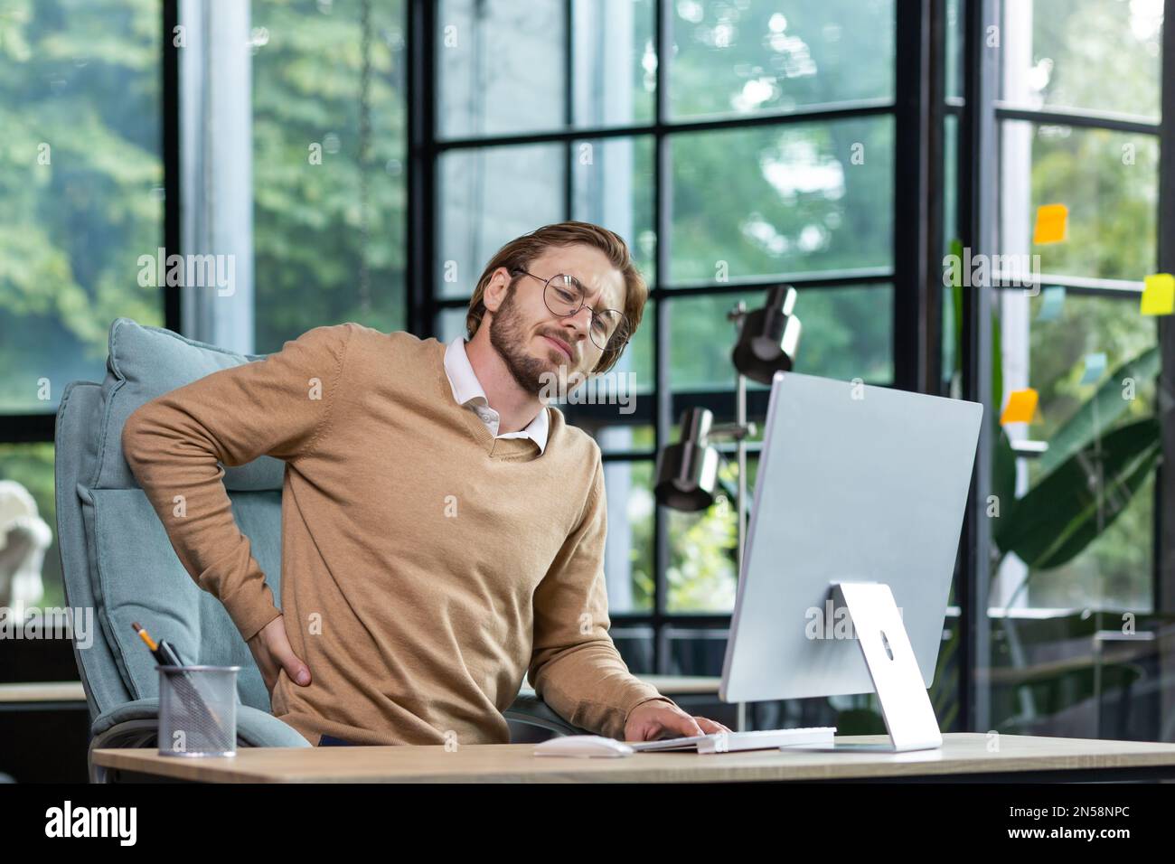 Tired businessman at workplace has severe back and lower back pain ...