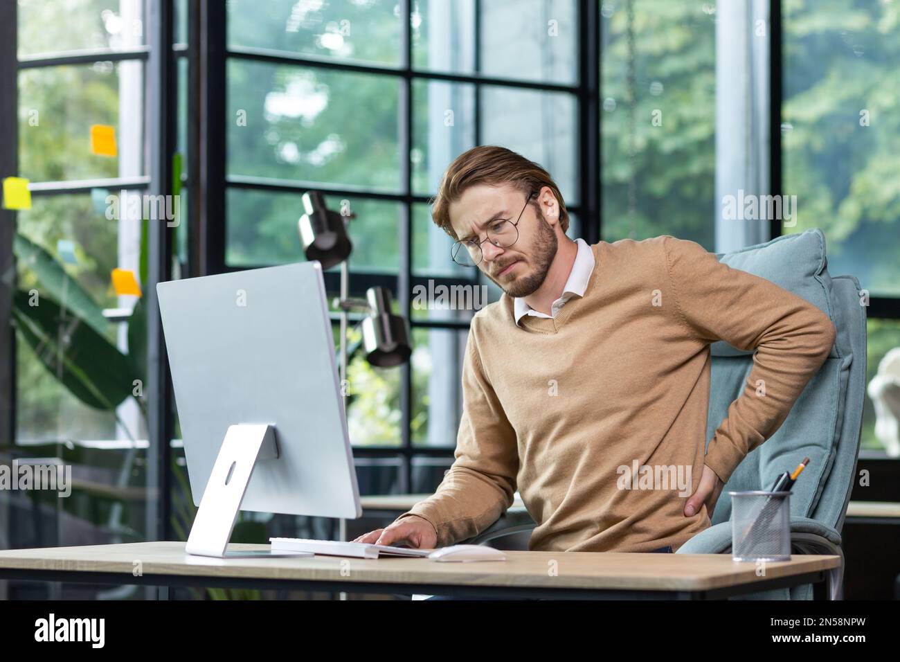 Tired businessman at workplace has severe back and lower back pain ...