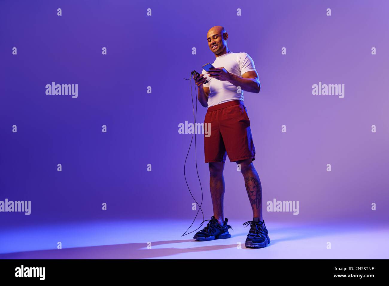 Young sporty man is check fitness app and holding jump rope standing on ...