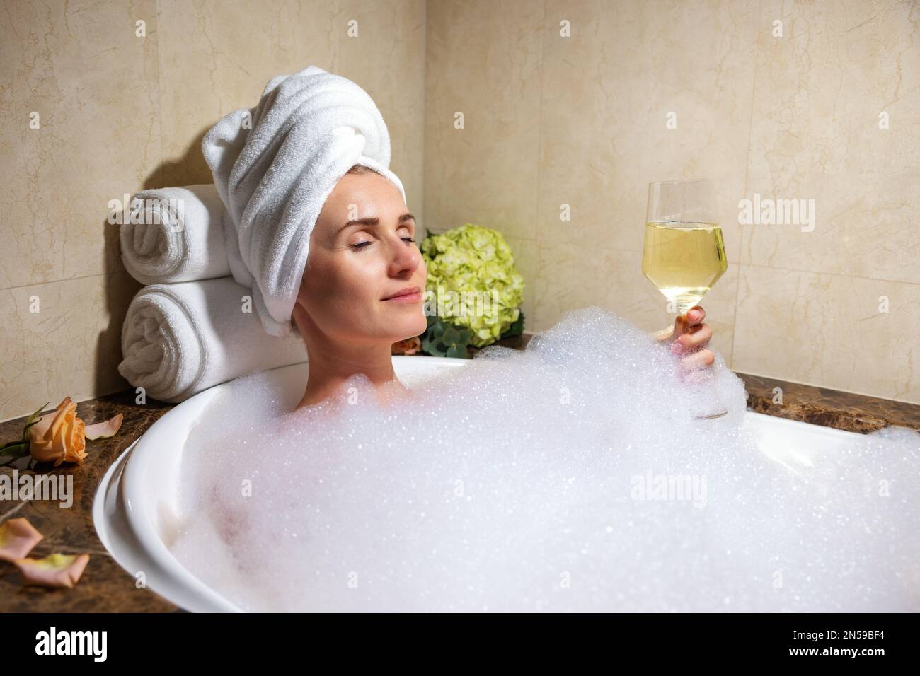 Woman Relaxing In Bath Full Of Foam With Glass Of Champagne In Spa