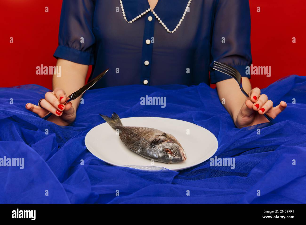 Cropped image of young girl cutting raw fish with knife over red ...