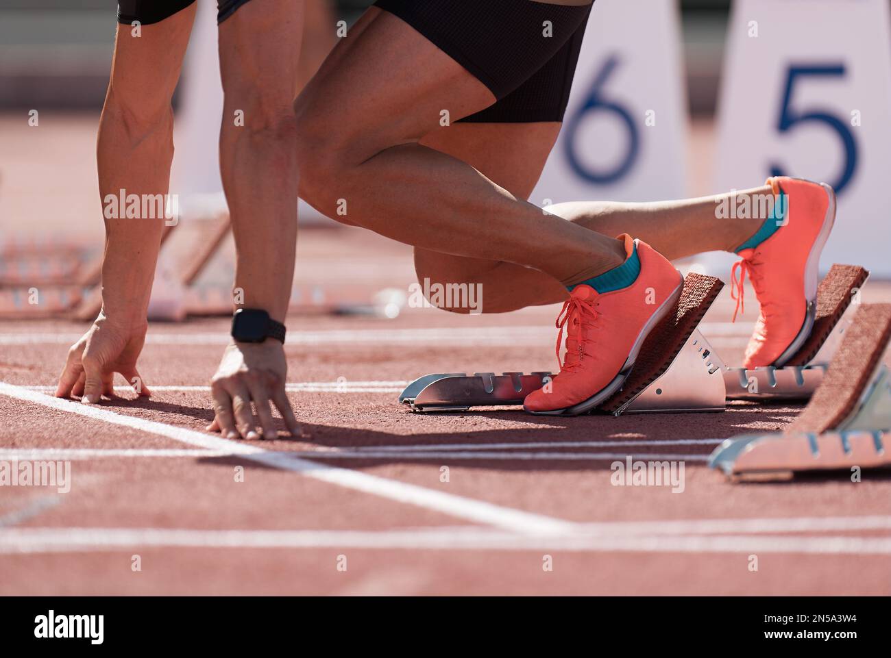 Man in a start block on an athletic track. A sprinter in a track and field race is poised at the ...