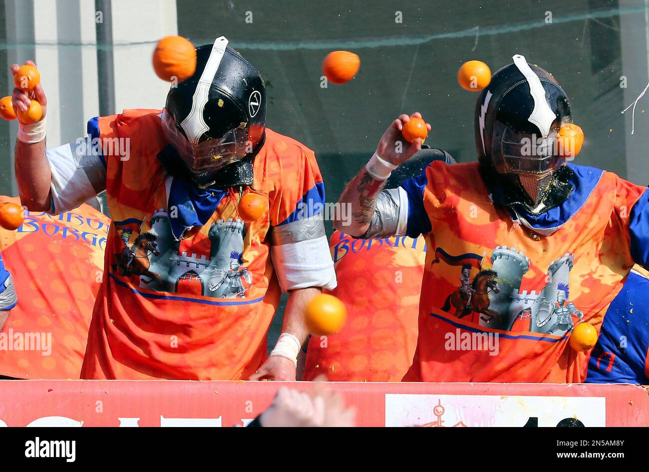 People wearing protection helmets and costumes throw oranges as part of ...