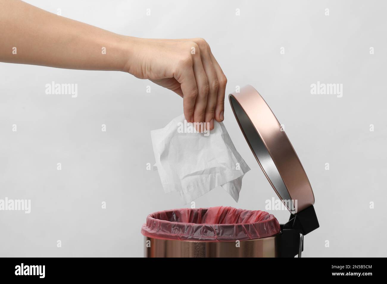 Woman putting paper tissue into trash bin on light background, closeup ...