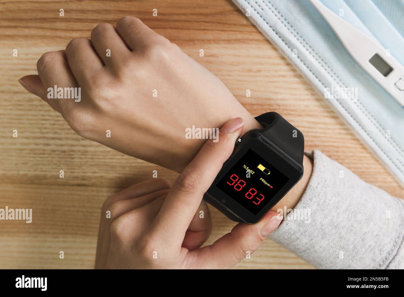 Woman measuring oxygen level with smartwatch at wooden table, top view ...