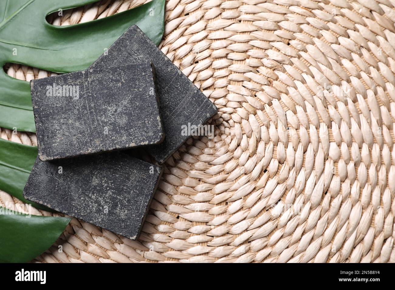 Natural tar soap on wicker mat with green leaf, flat lay. Space for ...