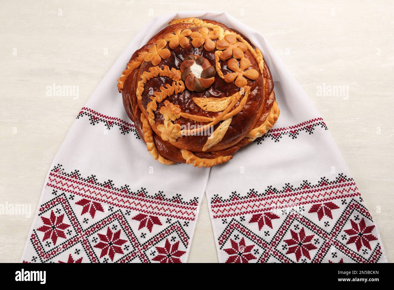 Rushnyk with korovai on white table, top view. Ukrainian bread and salt ...