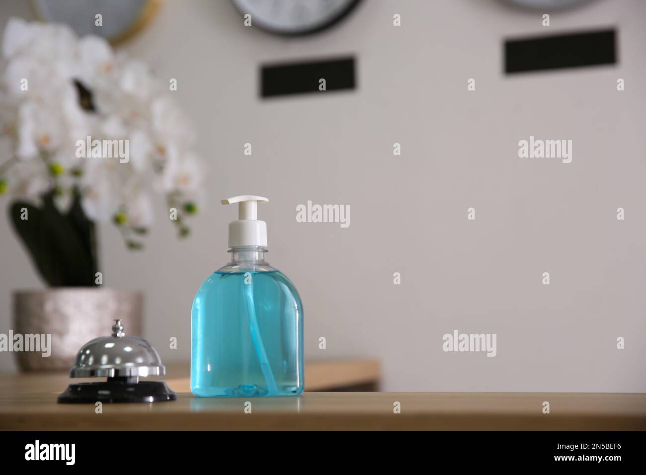 Dispenser bottle of antiseptic gel and service bell on reception desk ...