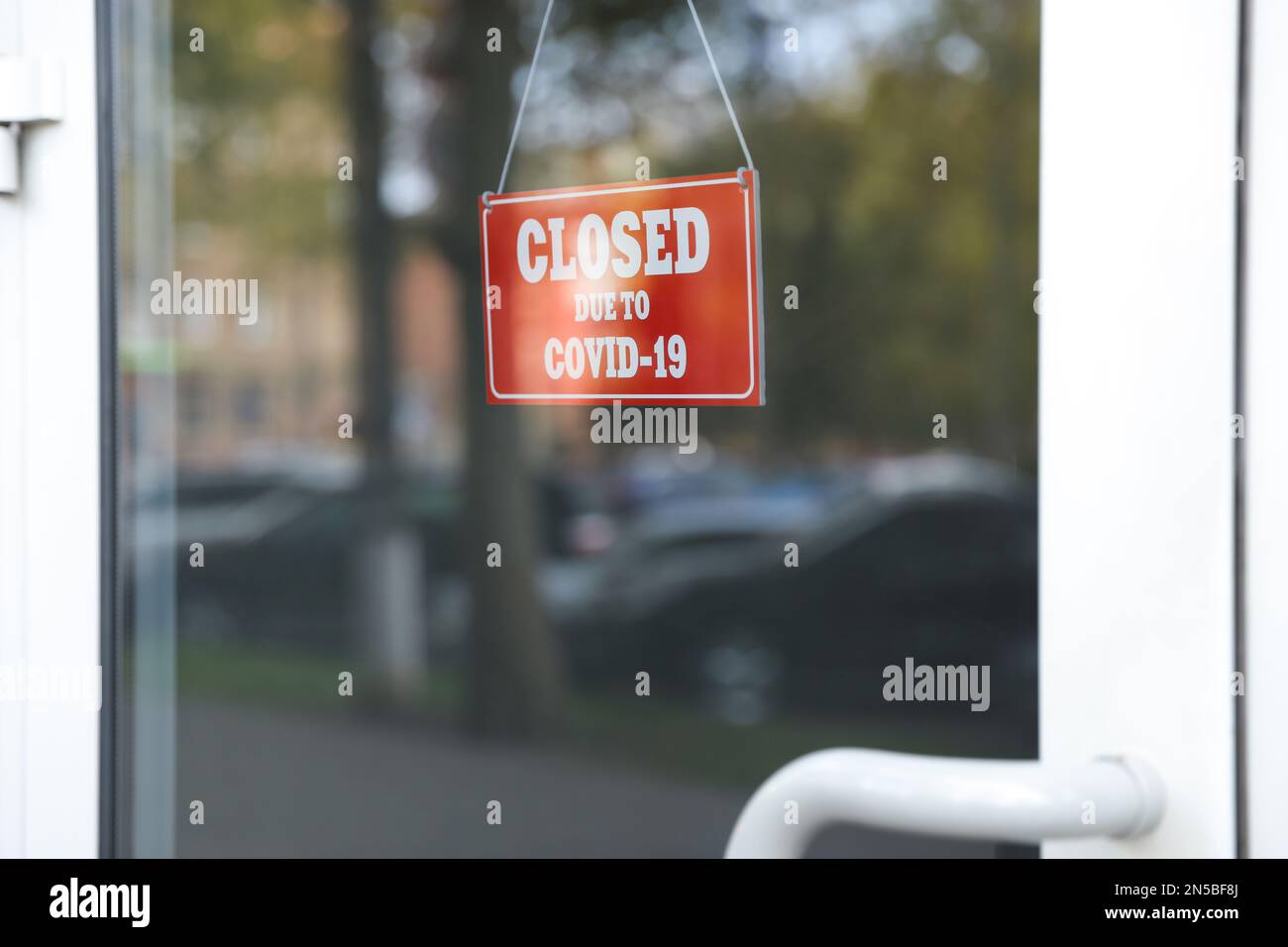 Red sign with words "Closed Due To Covid-19" hanging on glass door ...