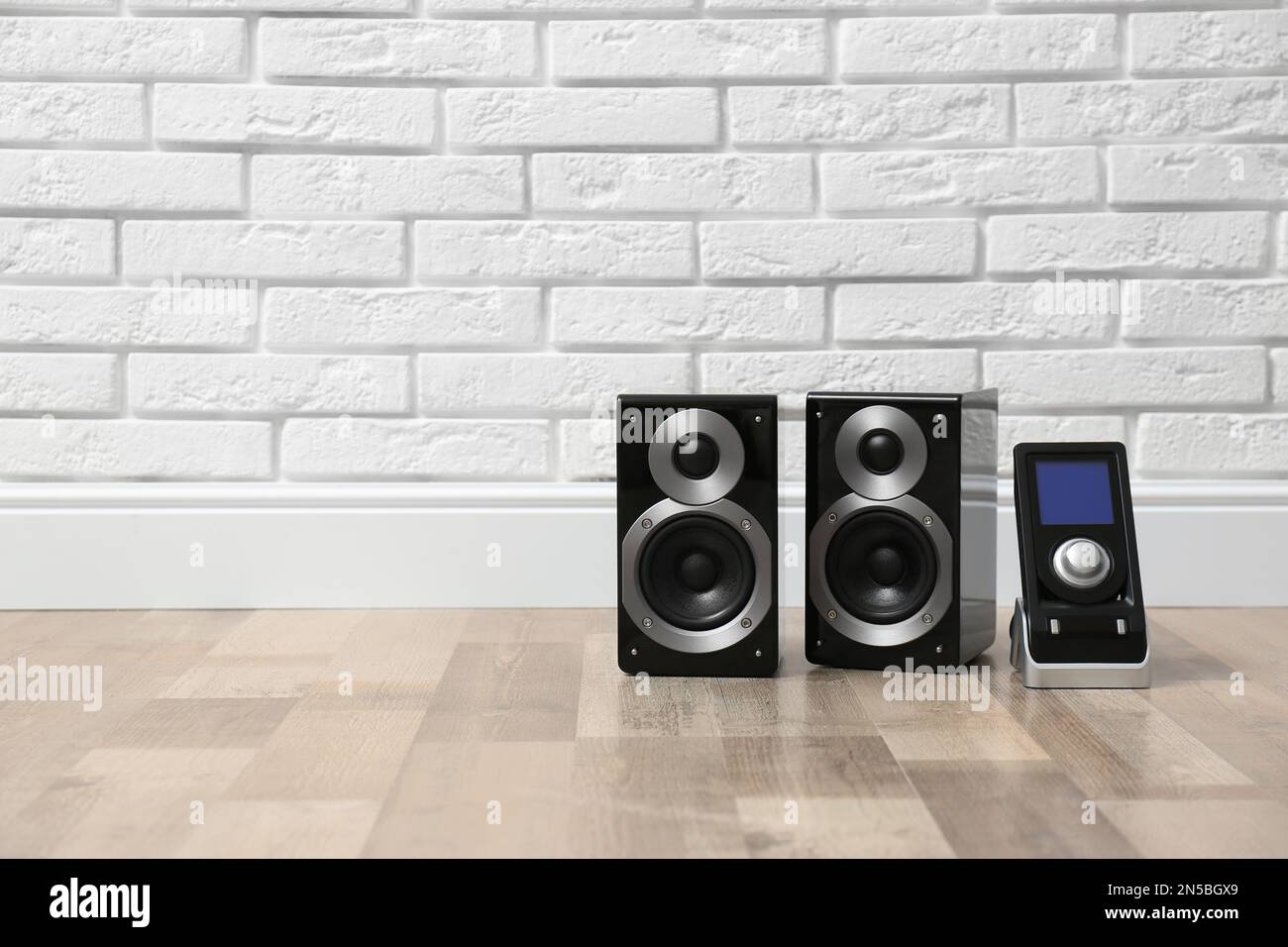 Modern powerful audio speakers and remote on floor near white brick ...
