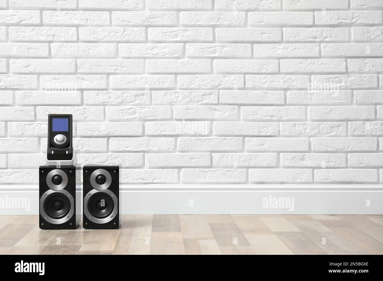 Modern powerful audio speakers and remote on floor near white brick ...