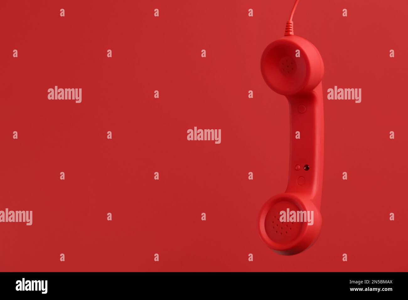 Corded telephone handset hanging on red background, space for text ...