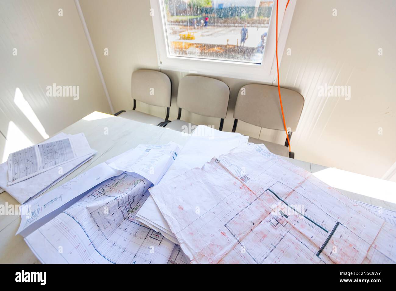 Mason's work desk in office container with pile of messy architectural ...