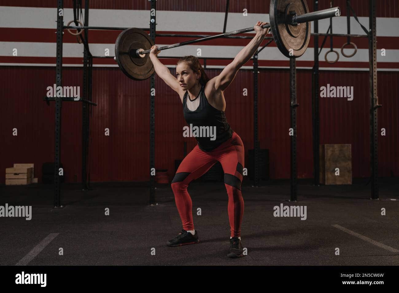 Young crossfit female athlete lifting heavy barbell overhead at the gym ...