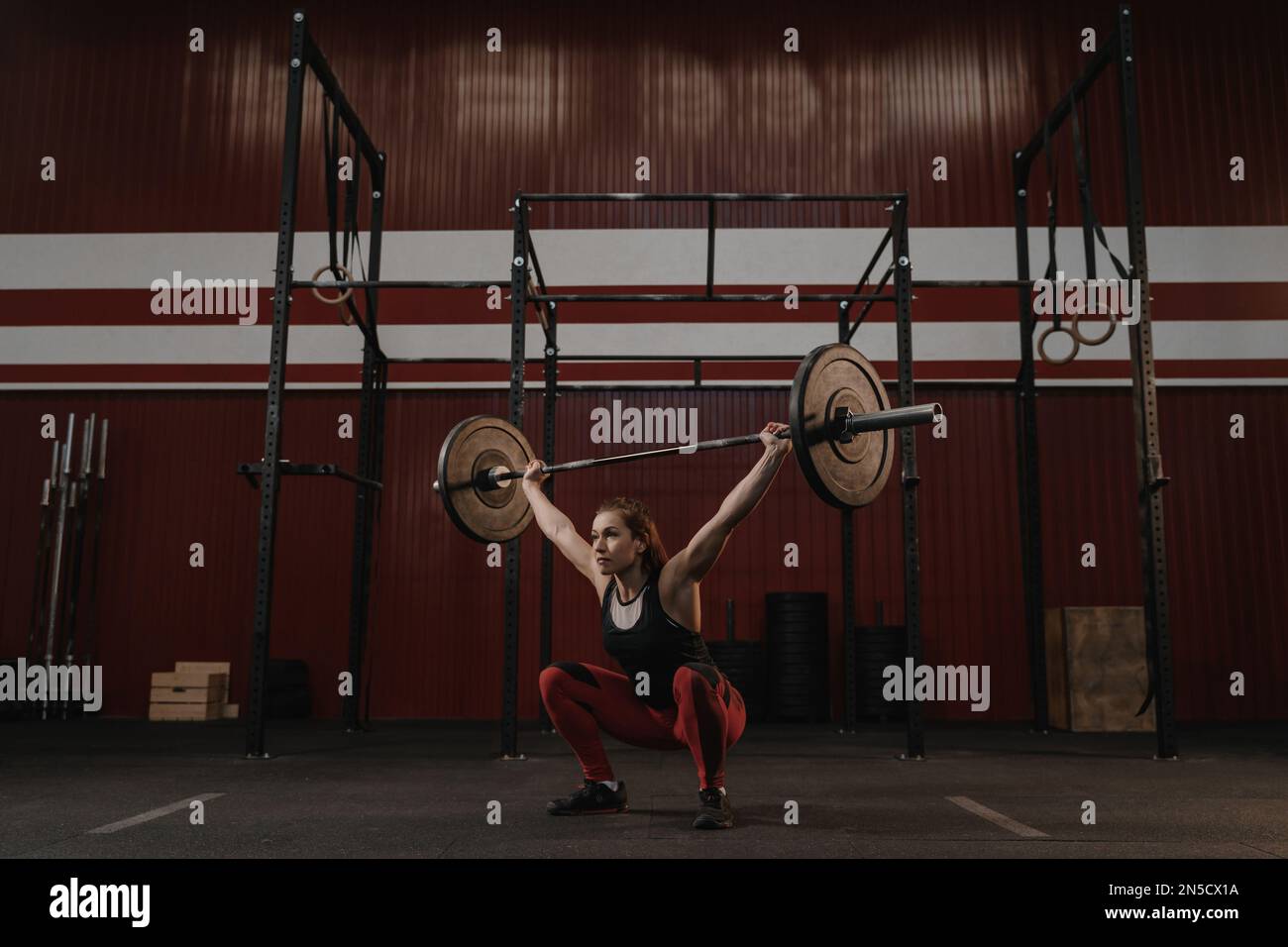 Strong crossfit woman doing squats with barbell overhead. Fit young woman lifting heavy weights ...