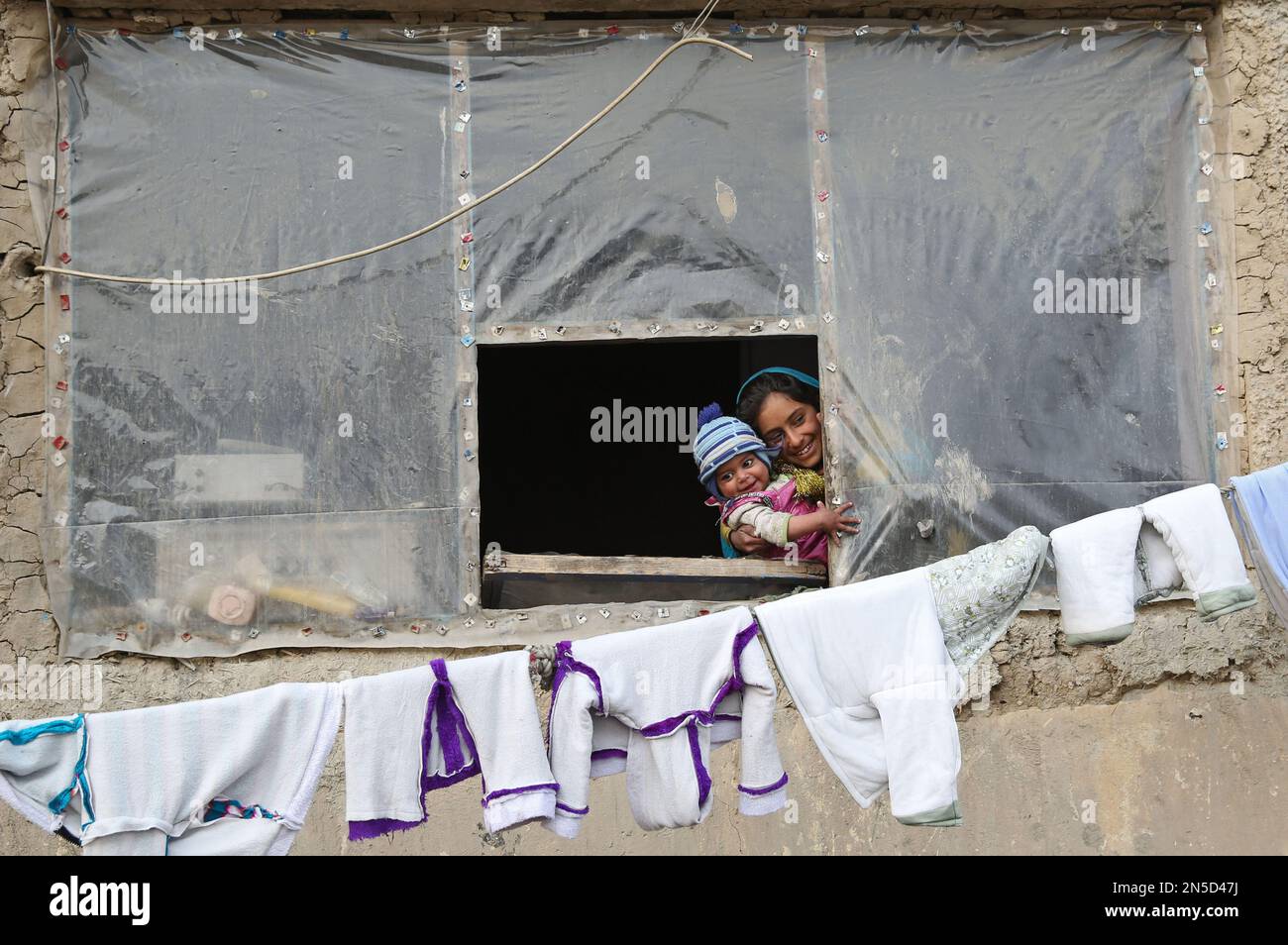 Afghan internally displaced girl holds a child as she peeks from a ...