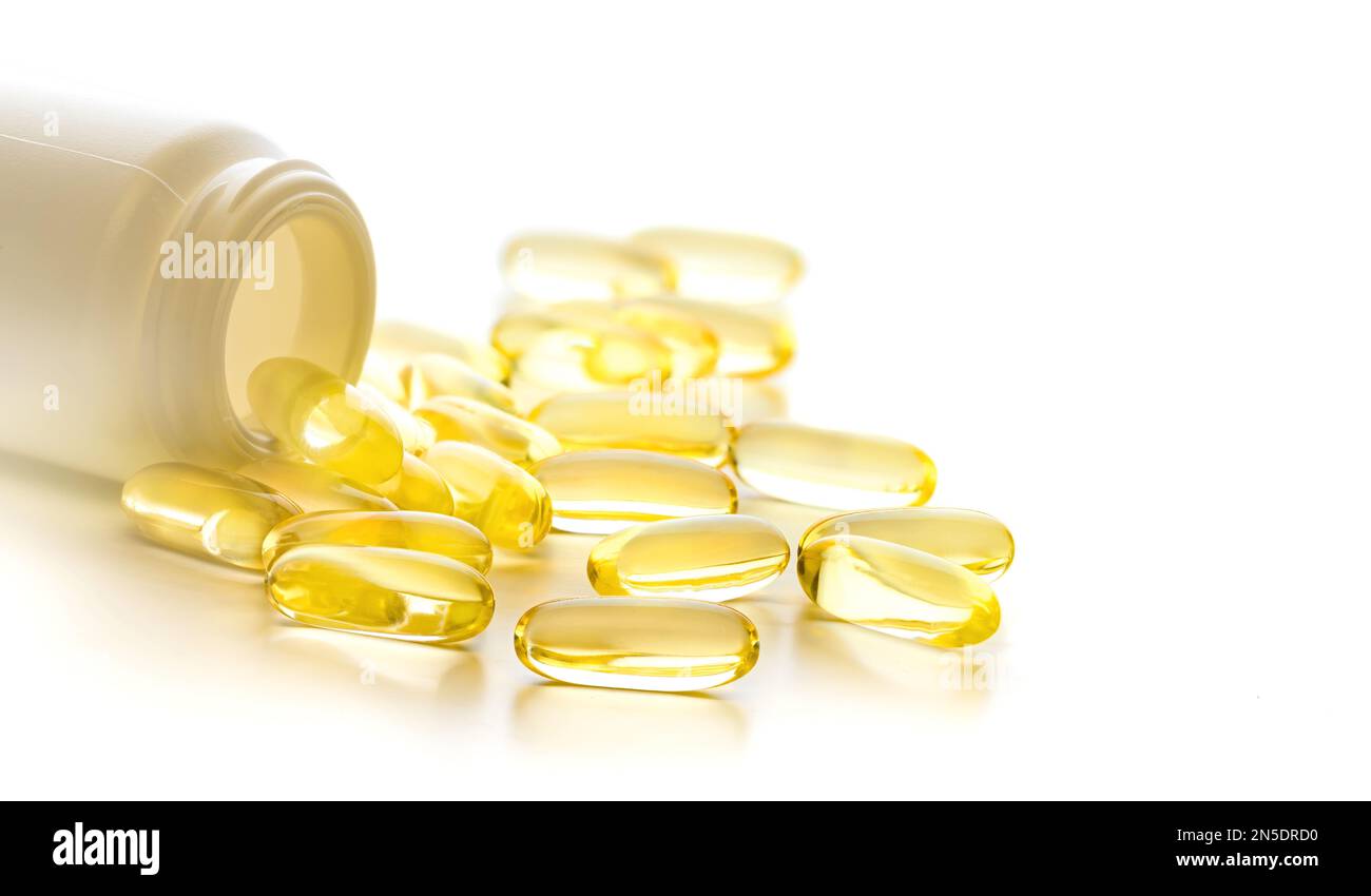 Yellow capsules of omega 3 pours from white plastic medicine container ...