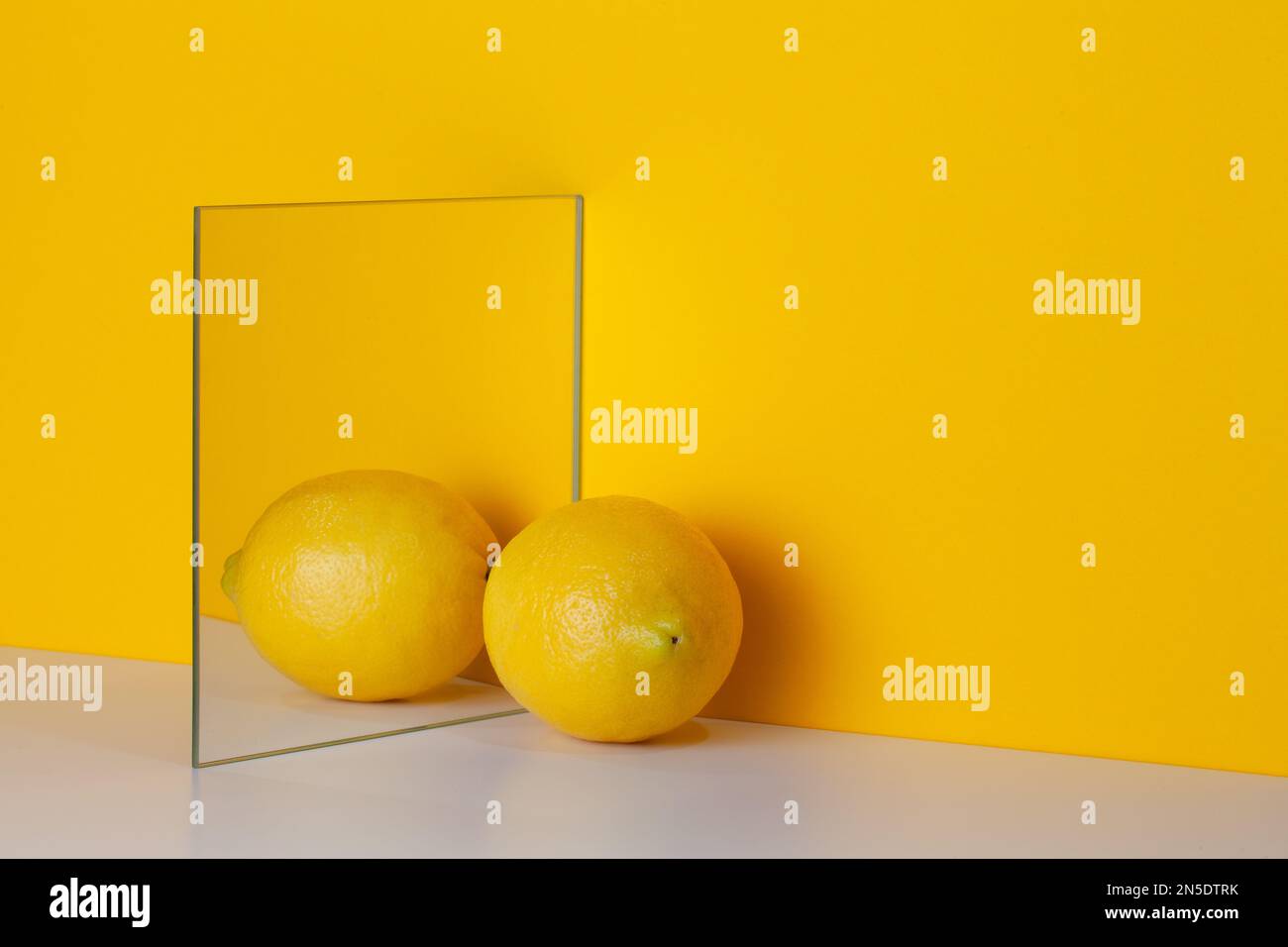 Yellow lemon is reflected in a mirror on a yellow background with copy ...