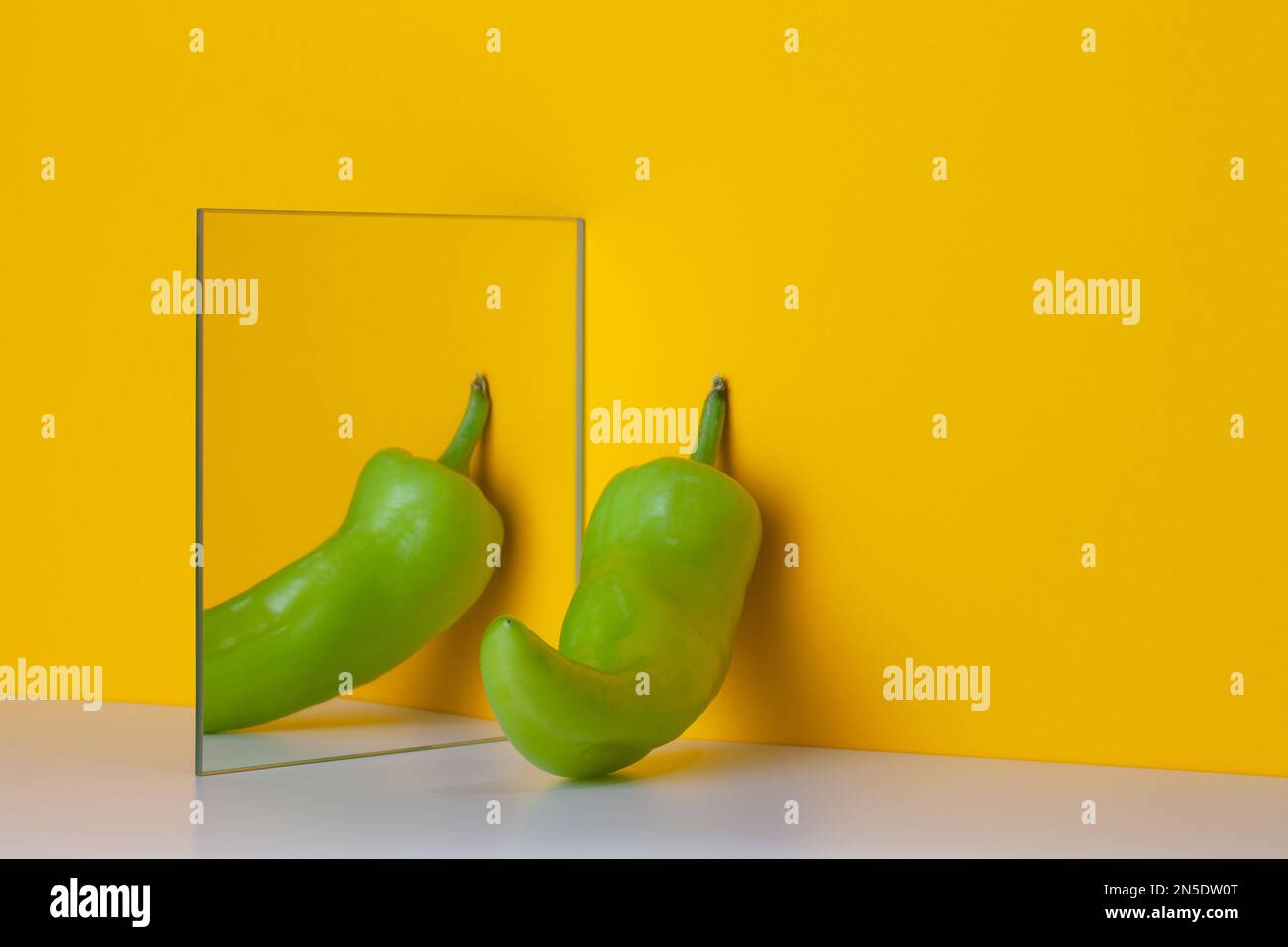 Green pepper is reflected in a mirror on a yellow background with copy ...