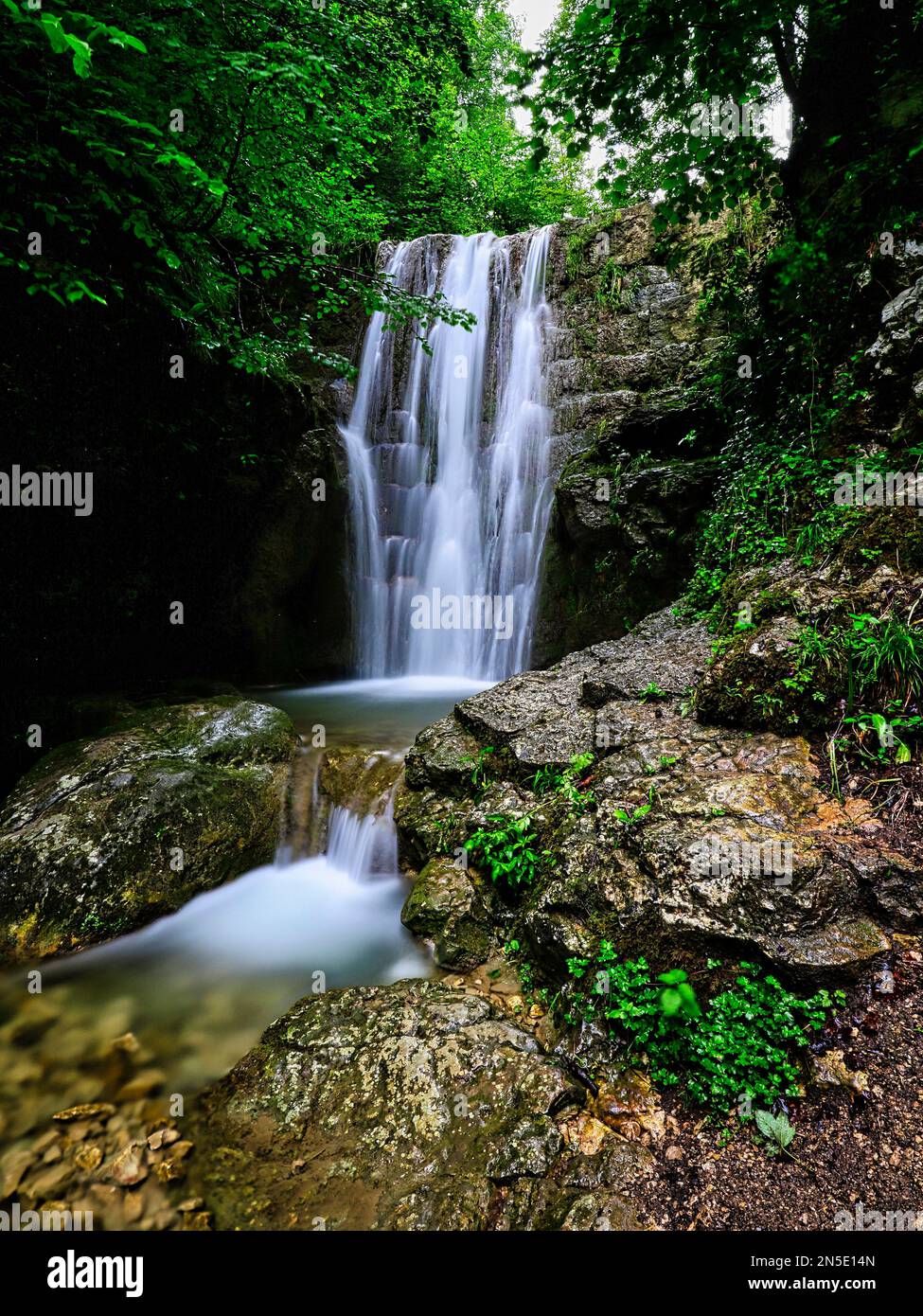 A vertical long exposure of a waterfall flowing into a river over the ...
