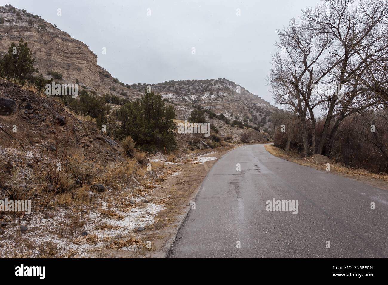 Road running alongside mountainside with snow patches under overcast ...