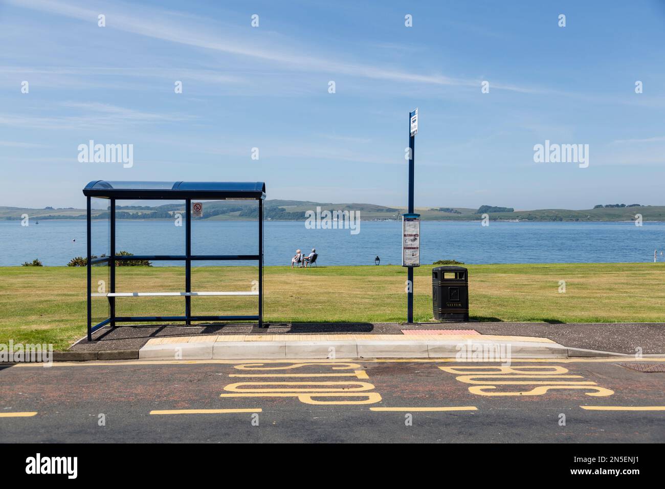 Couple sitting on deck chairs in the sun beside the Firth of Clyde in ...